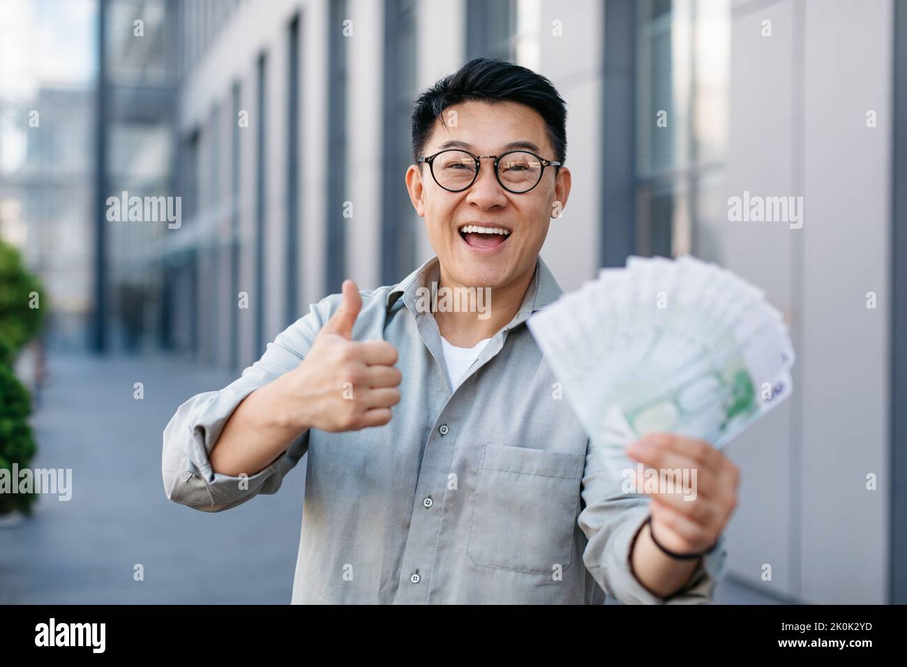 Overjoyed asian businessman holding fan of euro money and showing thumb ...