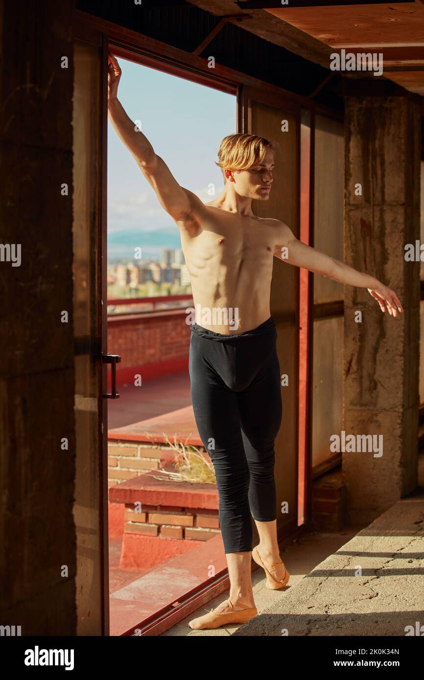 Amazing young gymnast in black leotard stretching the arm near window ...