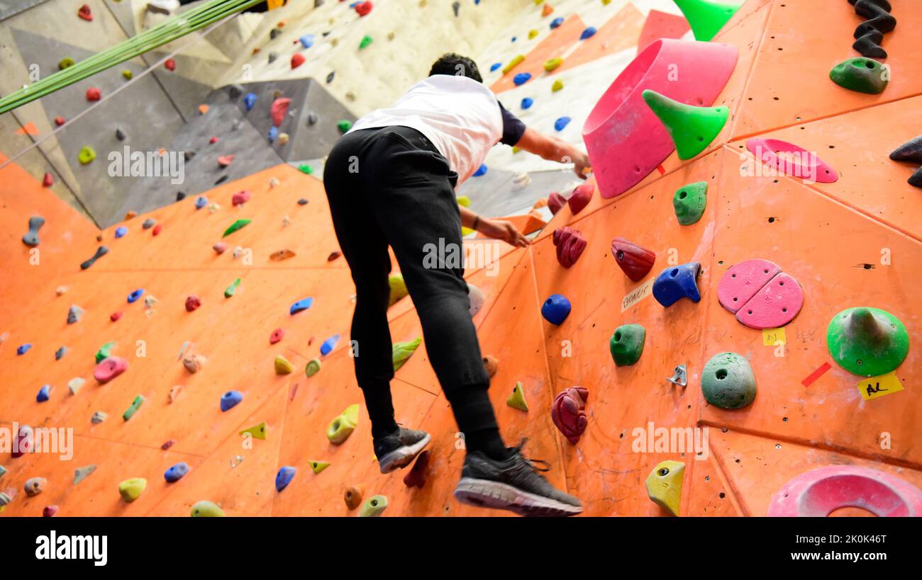 Young man climbing in an orange-colored rock climbing wall Stock Photo ...