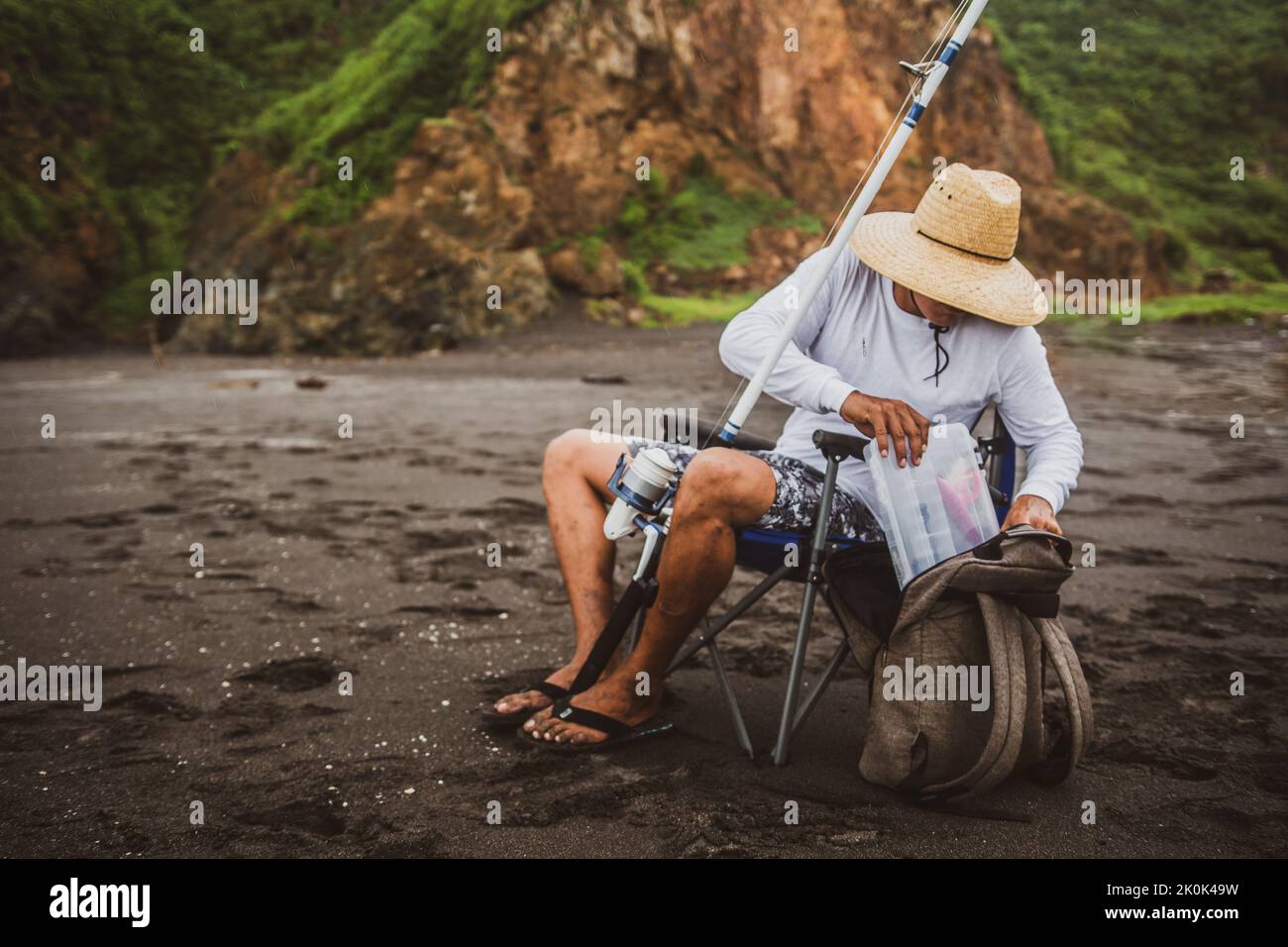 Full body of anonymous male in hat with fishing rod sitting on chair ...