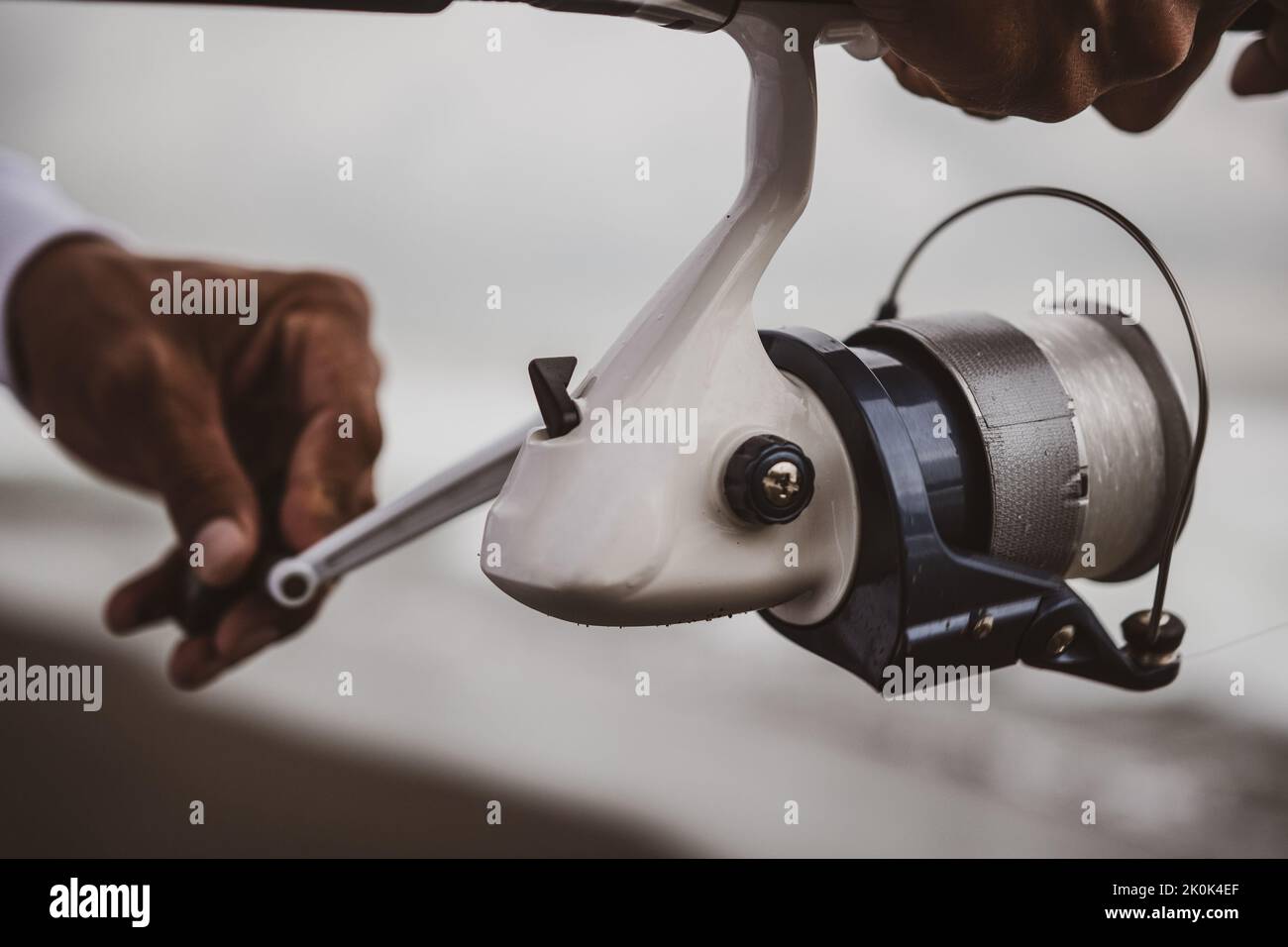 Crop anonymous man turning metal handle of special spinning reel ...