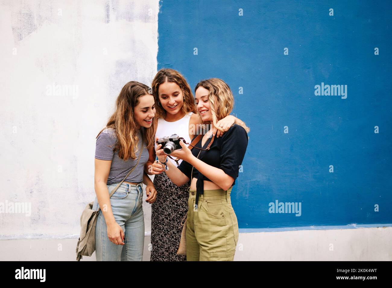 Charming friends hugging against wall while woman shows a picture on ...