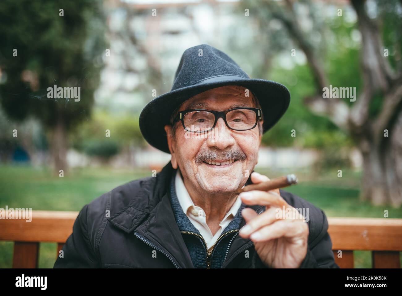 Cheerful senior male with mustache wearing hat smoking cigar and ...