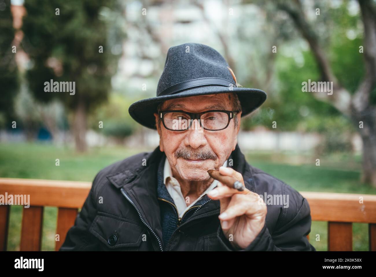 Happy senior male with mustache wearing hat smoking cigar and looking ...