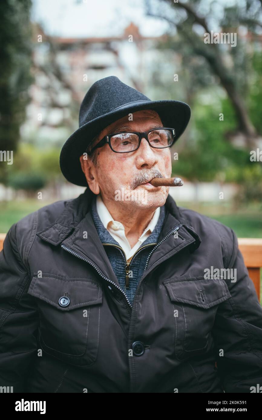 Senior male with mustache wearing hat smoking cigar and looking away ...