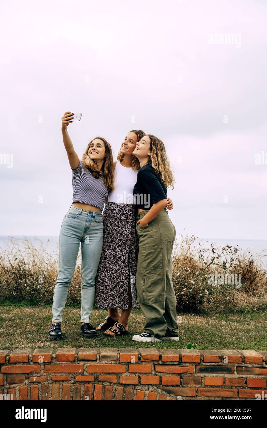 Cheerful smiling women hugging and taking selfie on mobile phone ...