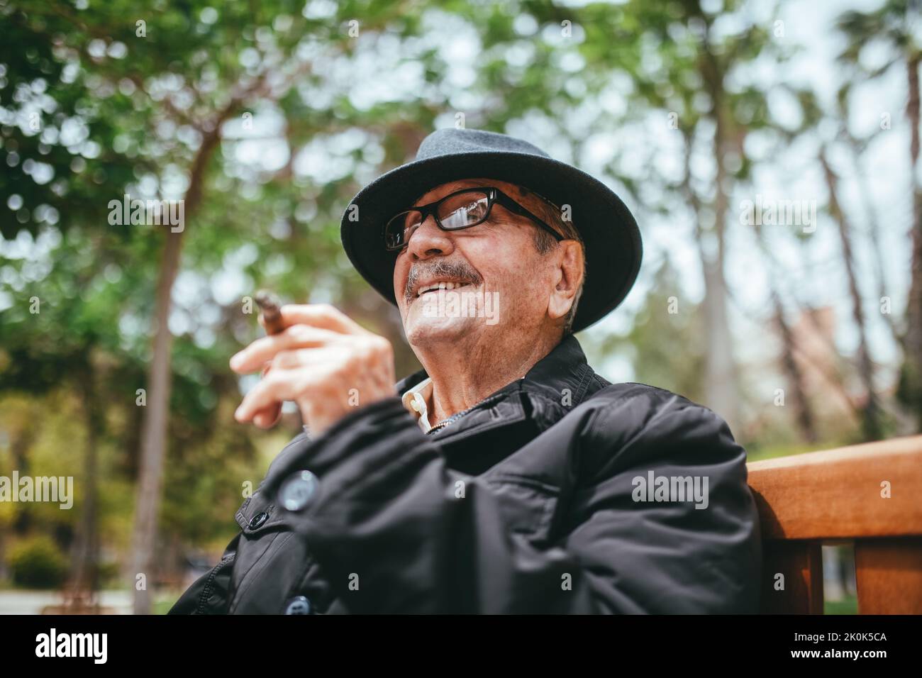 From below cheerful senior male with mustache wearing hat smoking cigar ...