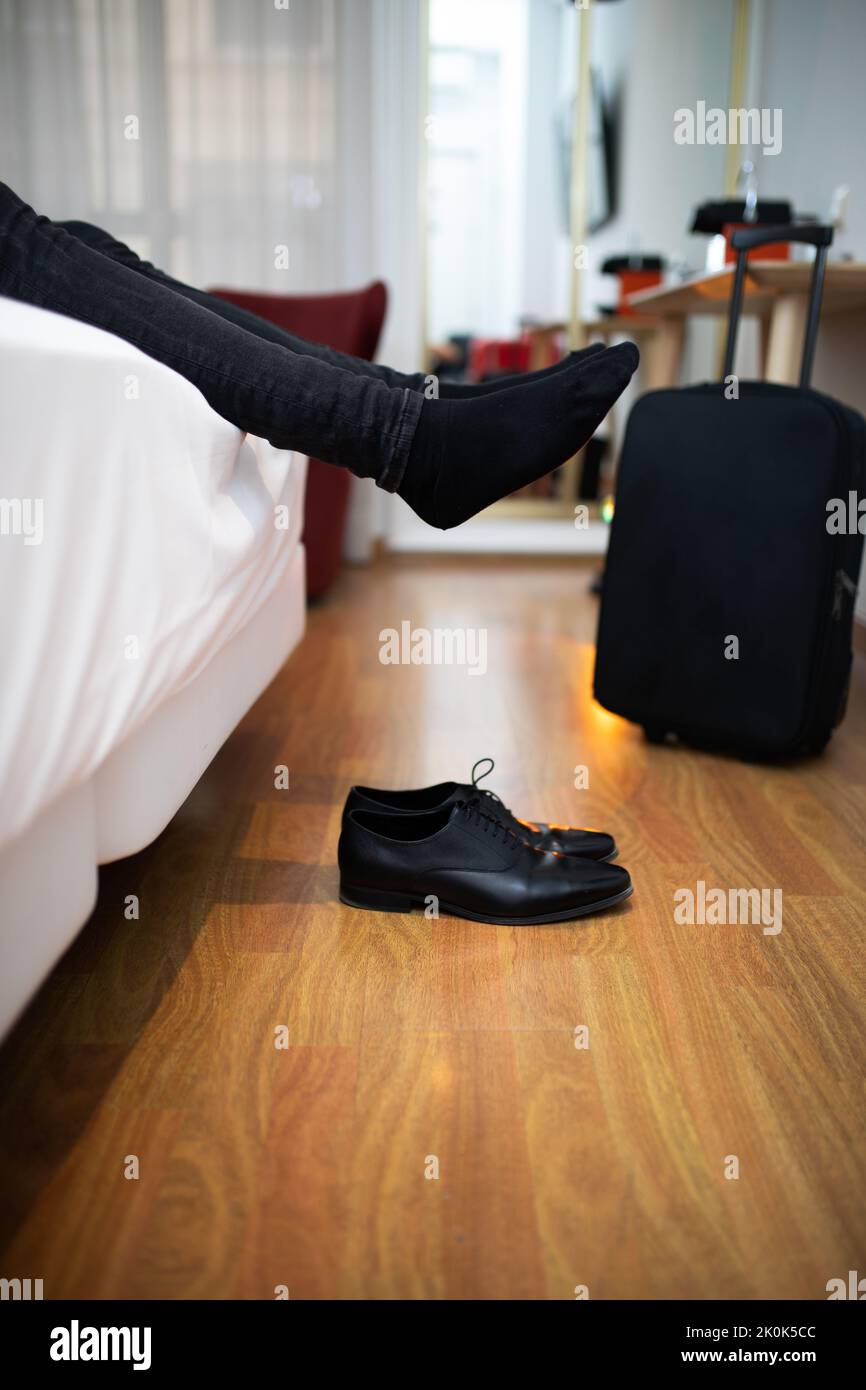 Crop tired male lying on comfortable white bed with shoes off in hotel ...
