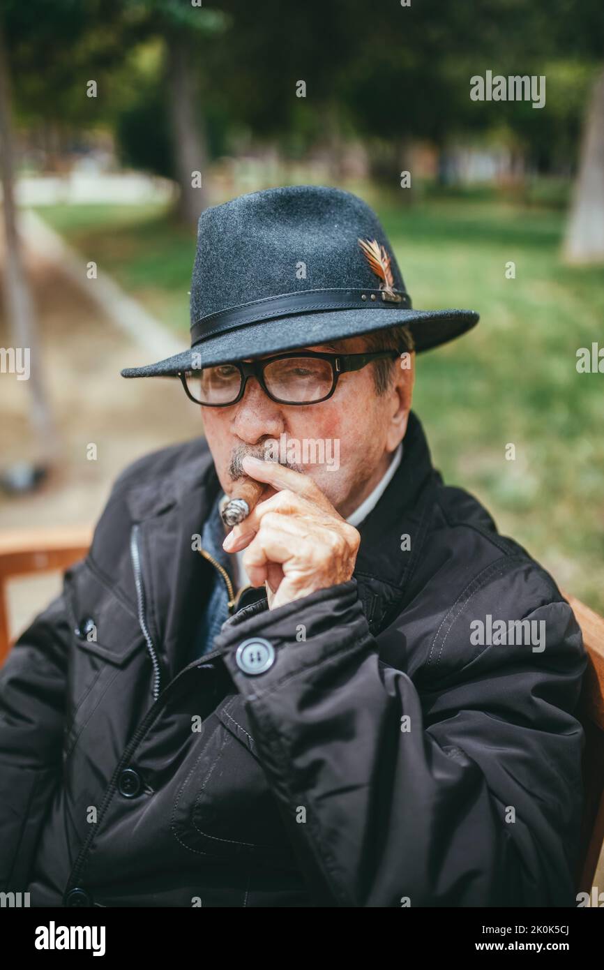 Senior male with mustache wearing hat smoking cigar and looking away ...
