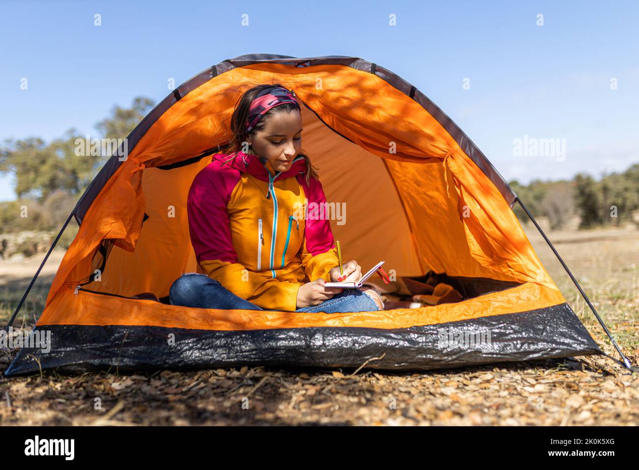 Focused young woman sitting in her tent writing notes on notebook while ...