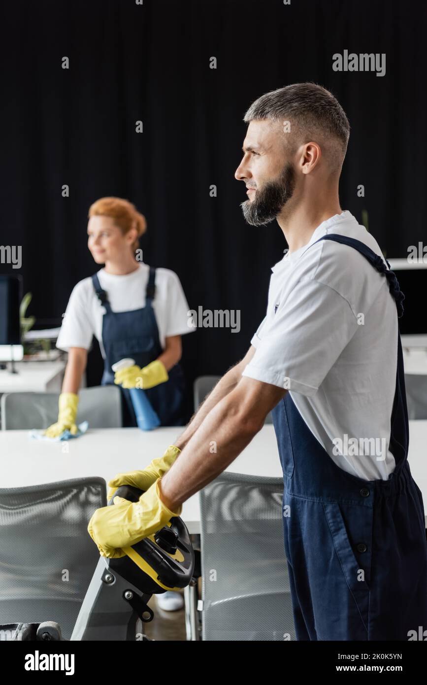 bearded man operating floor scrubber machine near woman working on ...