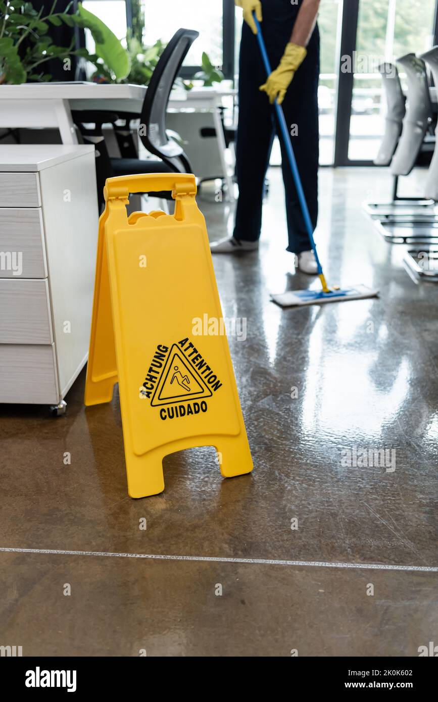 selective focus of caution board near cropped man washing floor with ...