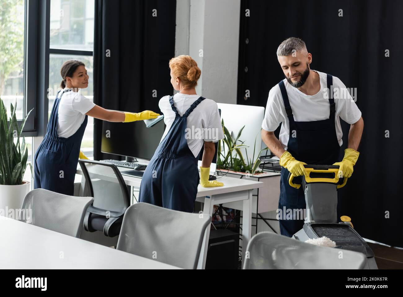 young bi-racial woman wiping computer monitor near colleagues cleaning ...