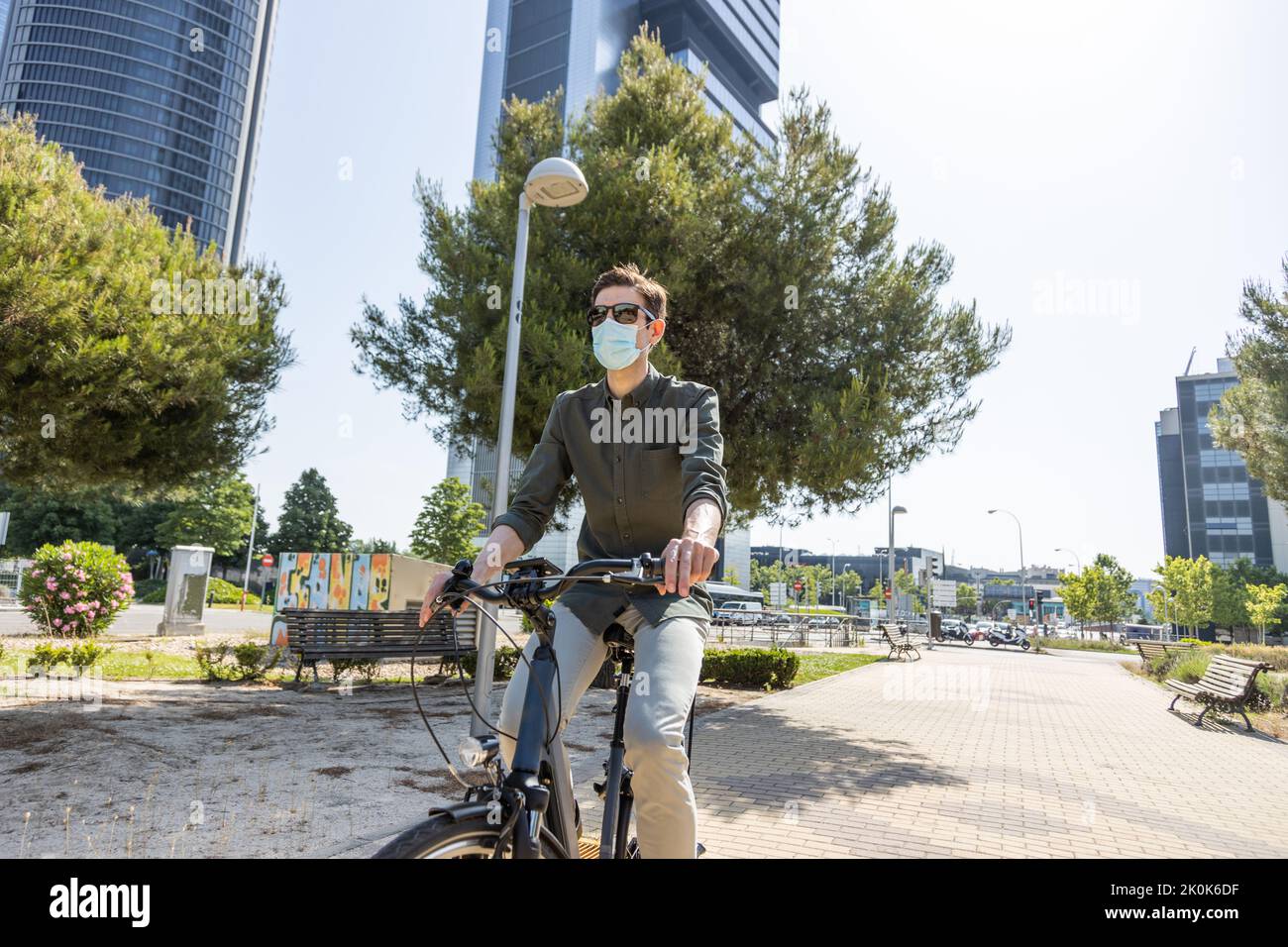 Male in protective mask riding contemporary bike along street while commuting to work in ...