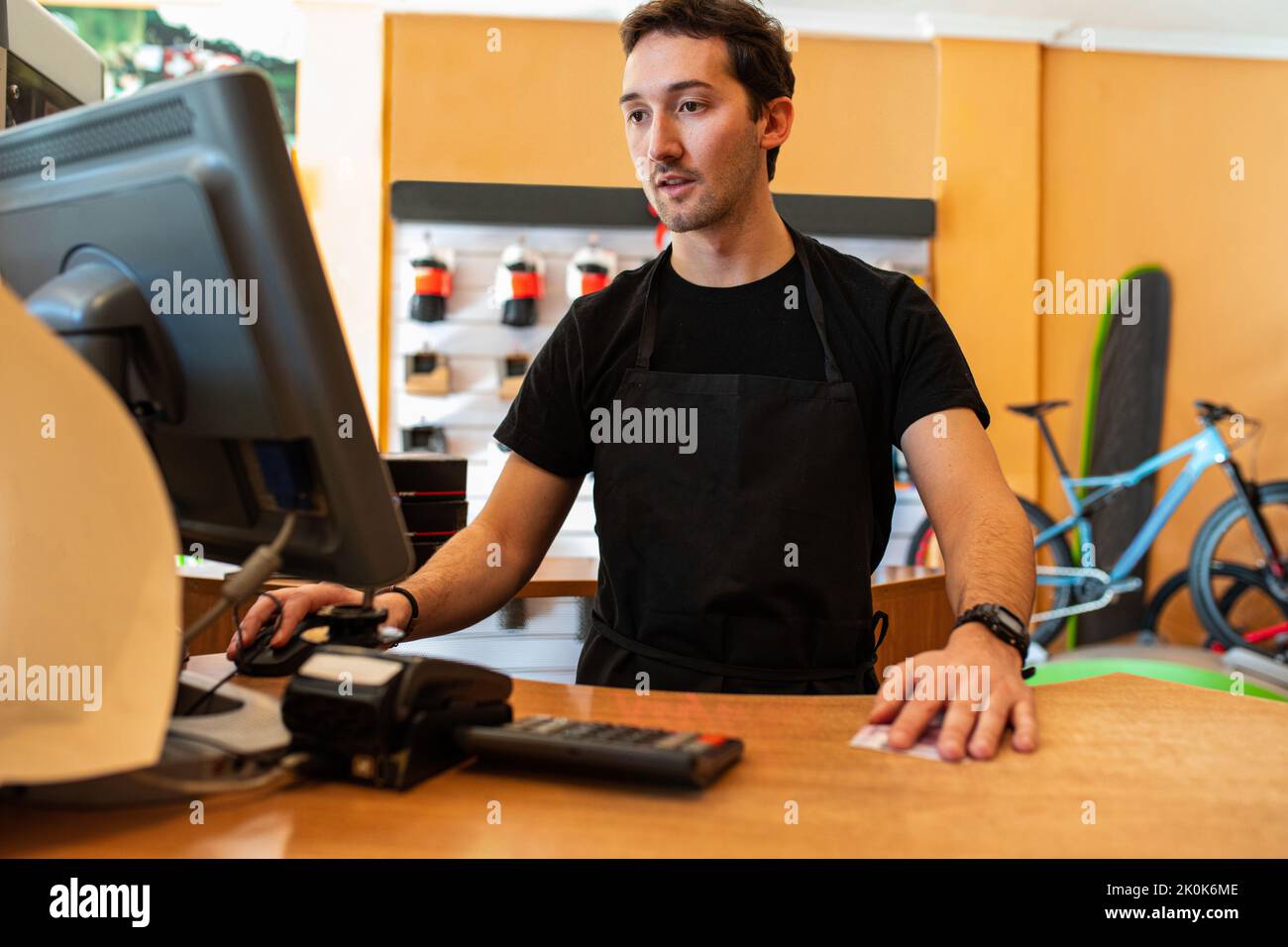 Happy young cashier in black t-shirt smiling and using computers while ...