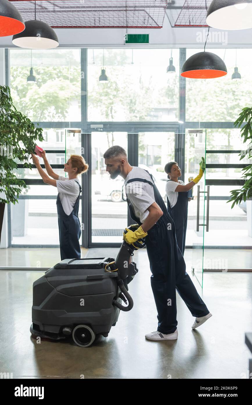 side view of man with floor scrubber machine near multicultural women ...