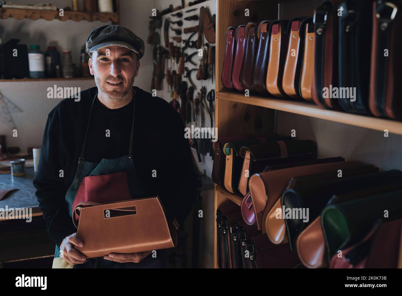 Craftsman standing in dark workshop holding leather bag looking at ...