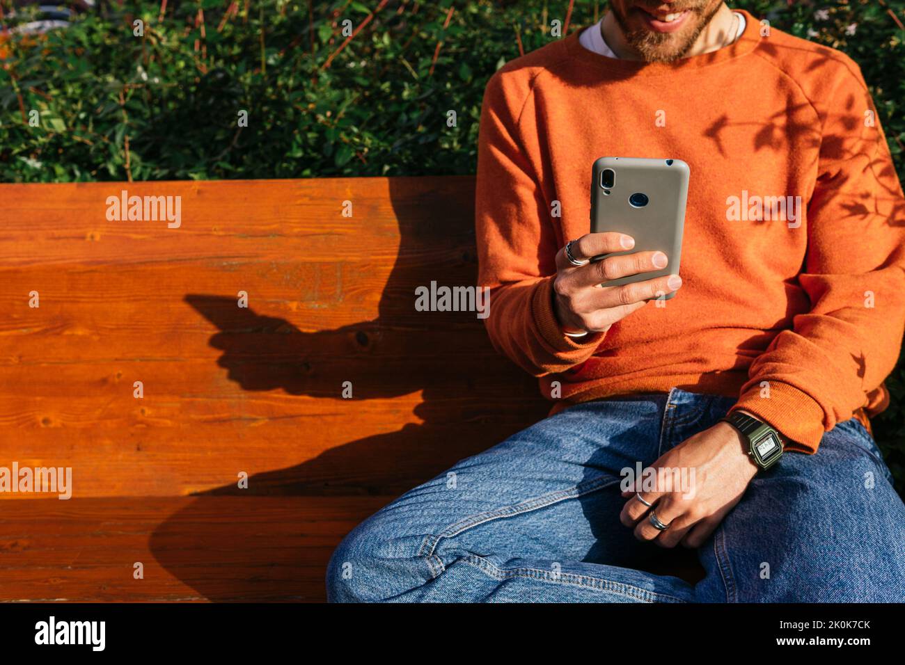 Cropped unrecognizable male in cap surfing internet on cellphone while ...