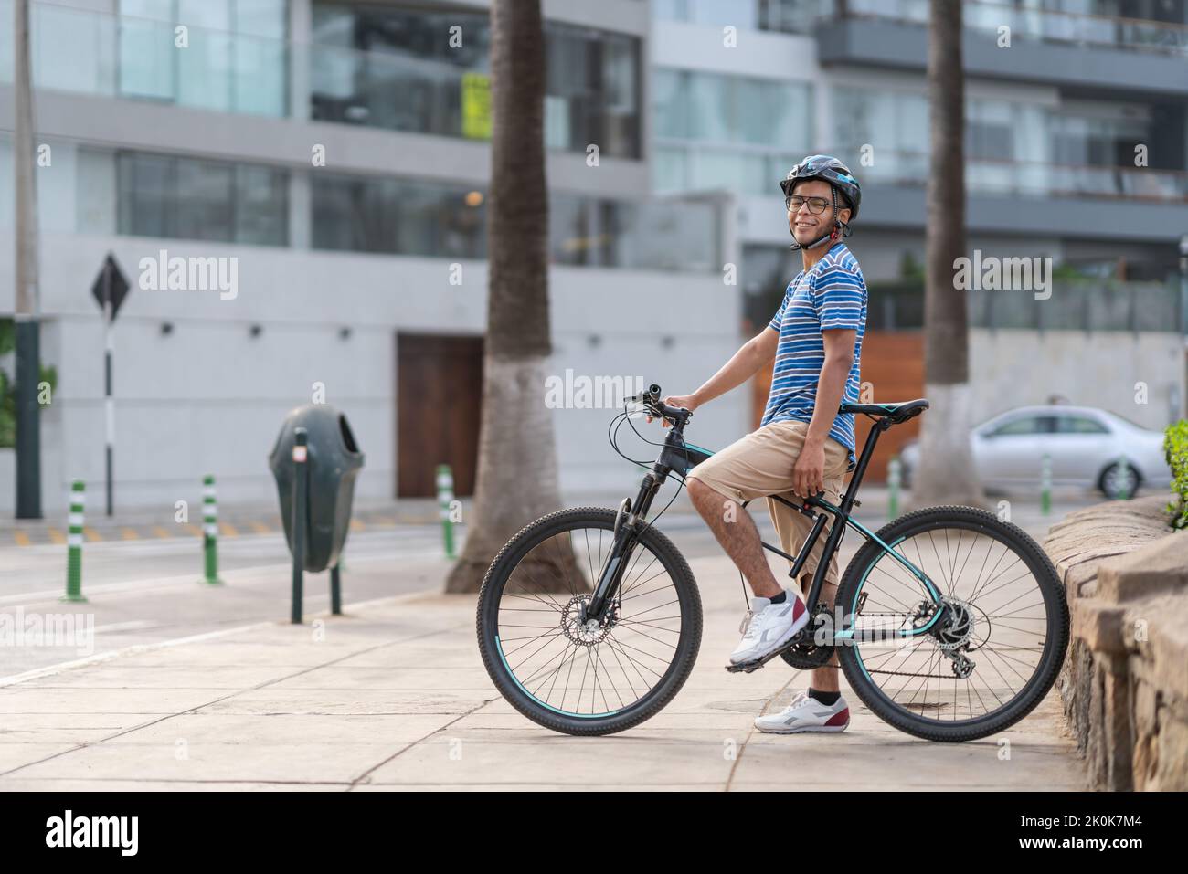 Full body of smiling ethnic male in casual wear riding bicycle on ...