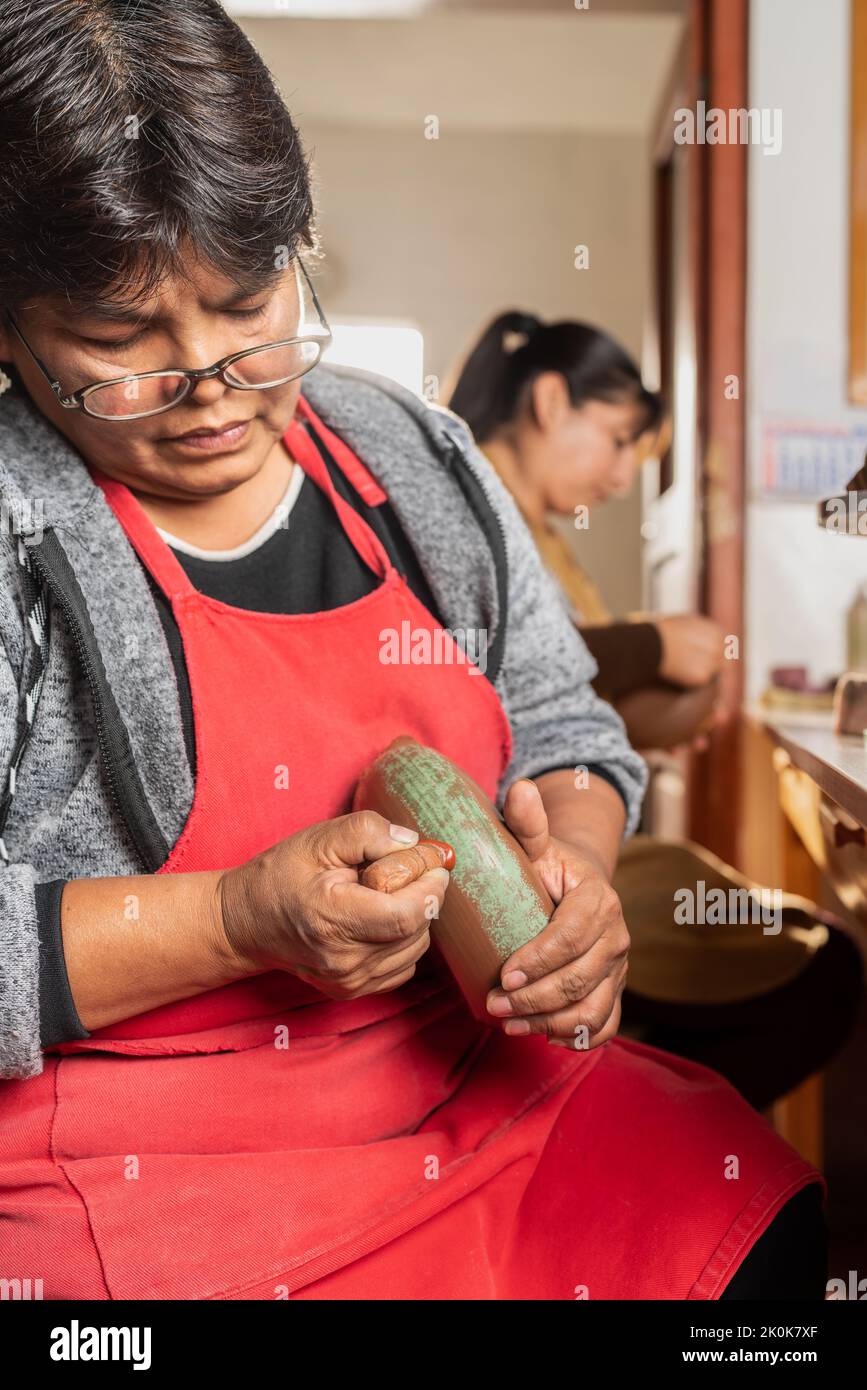 Concentrated Peruvian female artisan in apron painting ceramic bowl ...