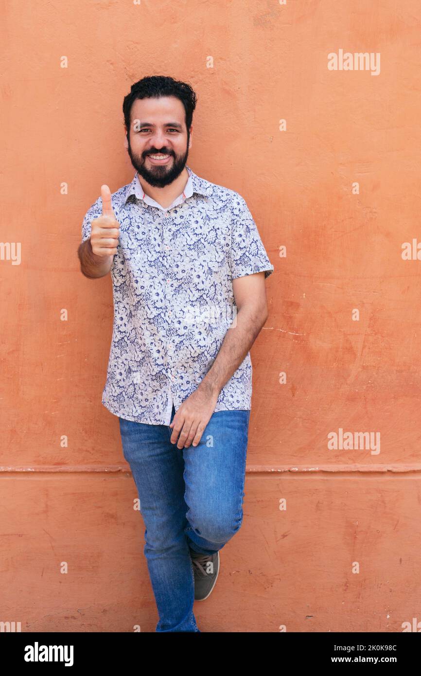 Delighted ethnic male showing like gesture while standing near peach ...