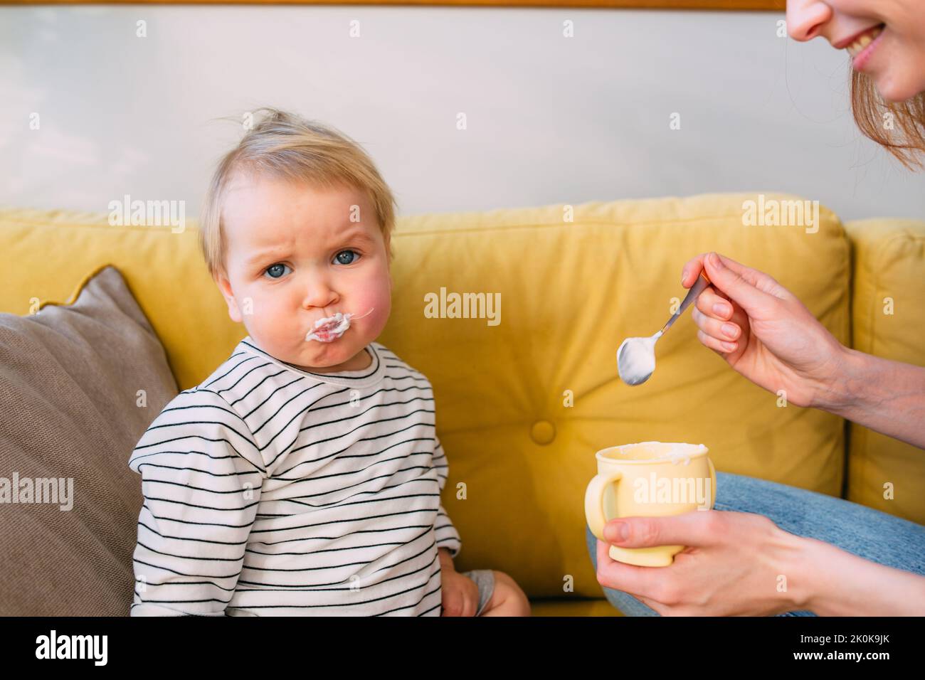 Mom feeds a small child at home with yogurt from a spoon. Family ...
