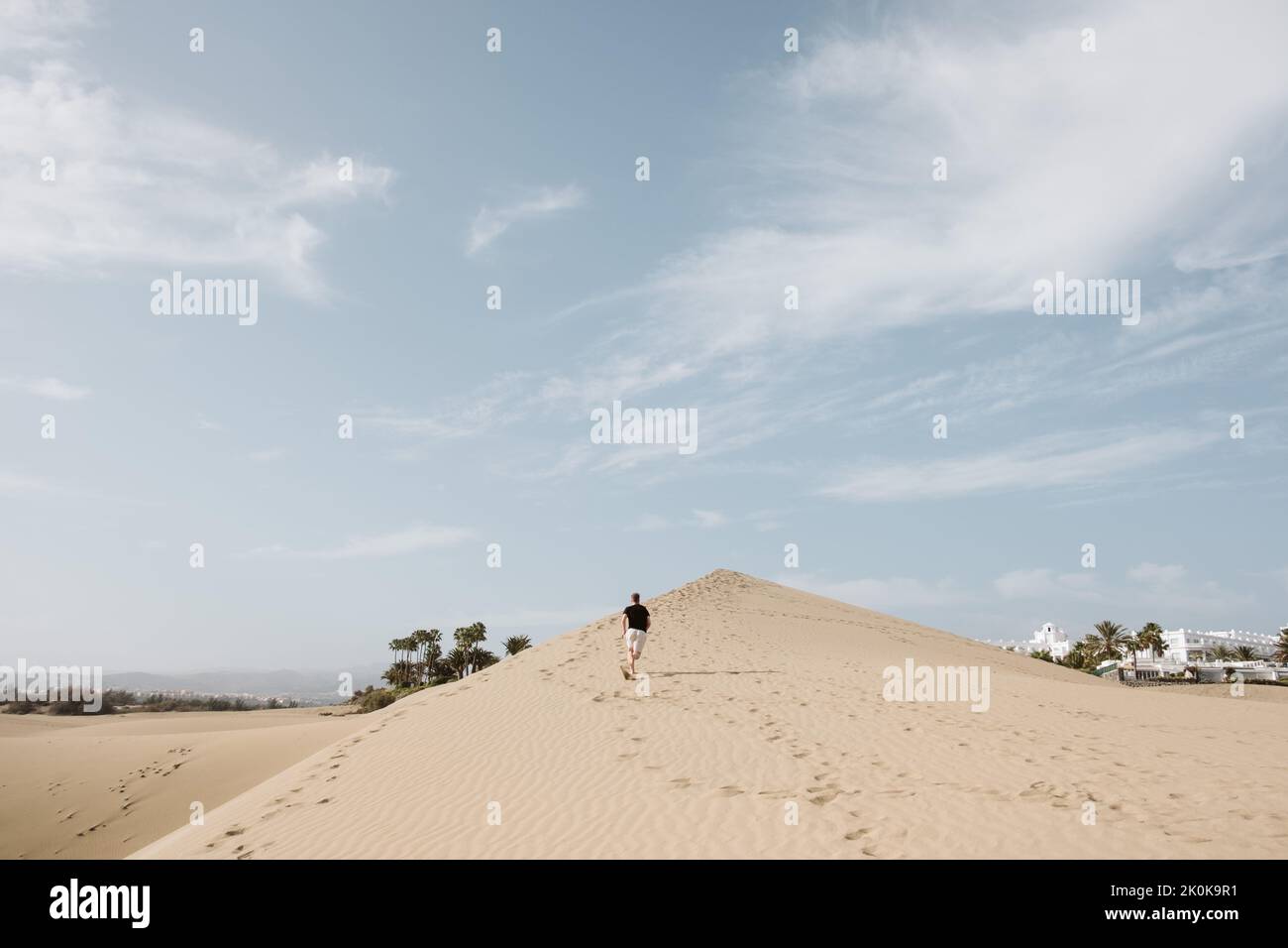 Back view of young man running on sand dune between desert and blue ...