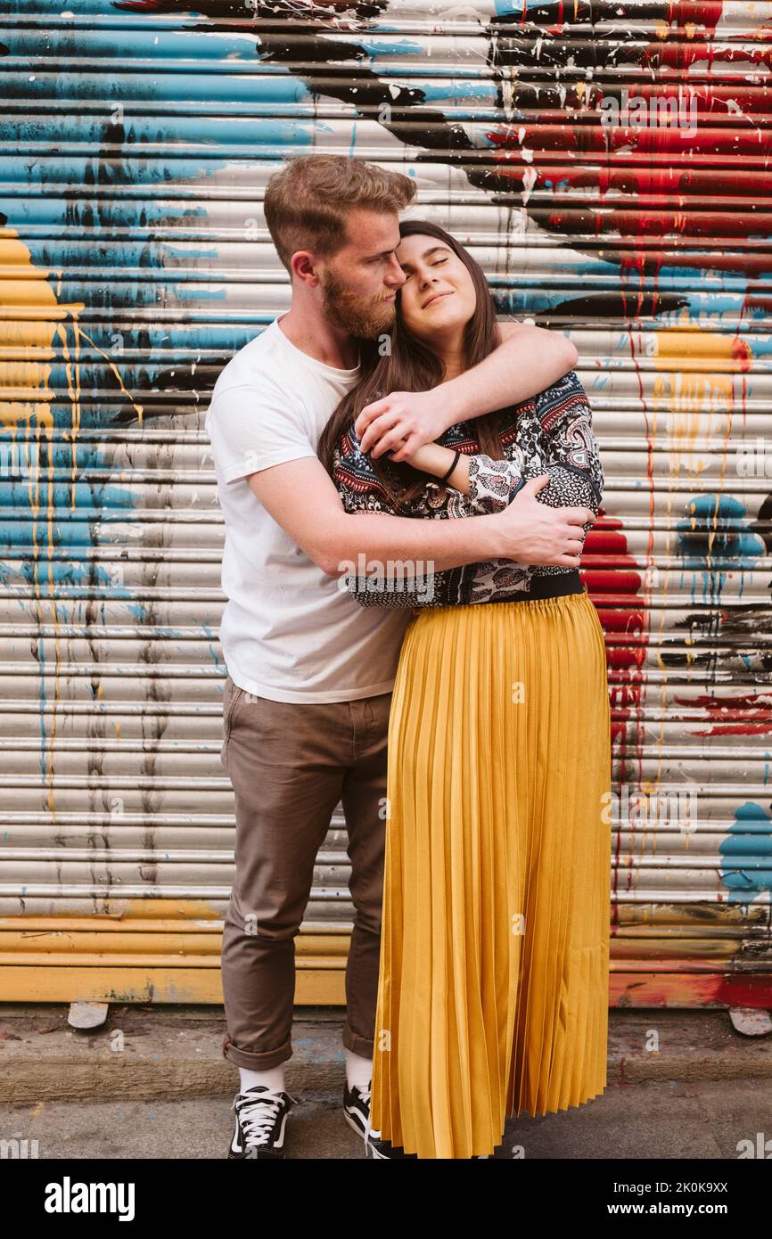 Side view of a couple hugging against a colored blind on the street ...