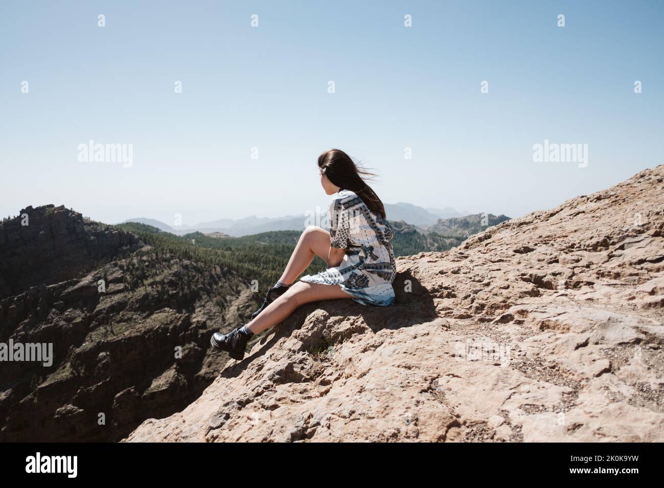 Side view of a woman sitting in a mountainous landscape while looking ...