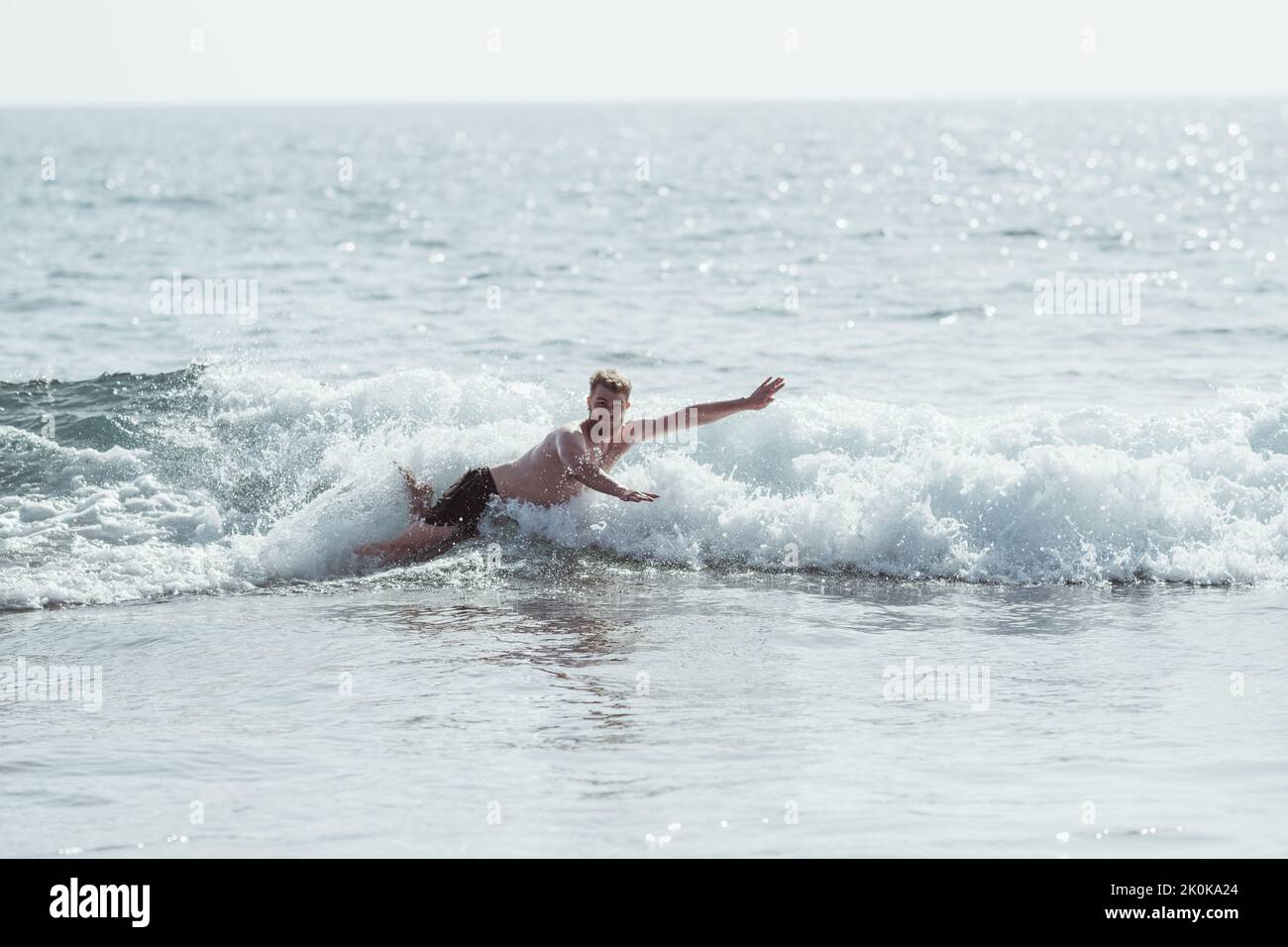 Young man doing a belly flop at beach splashing water in summertime ...