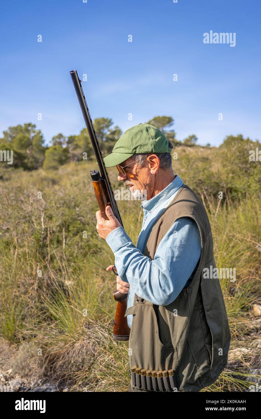 Side view of male hunter in special hunting vest and green cap holding ...