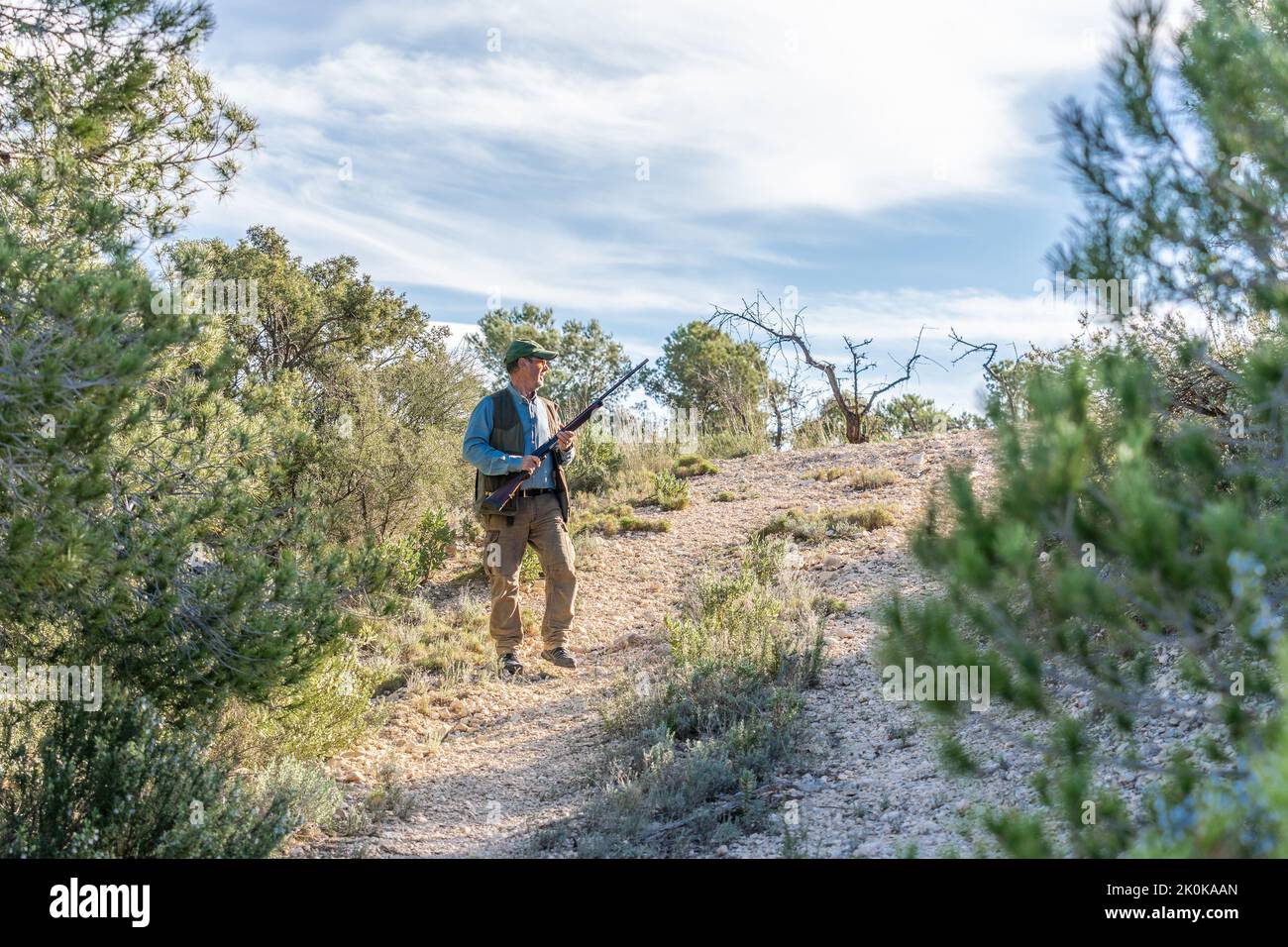 Male hunter in special hunting vest and green cap holding rifle and ...