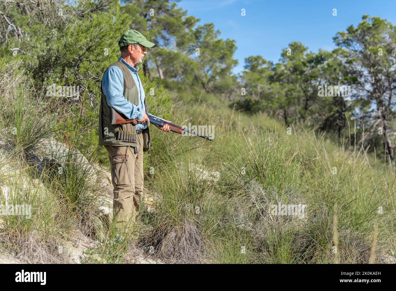 Side view of male hunter in special hunting vest and green cap holding ...