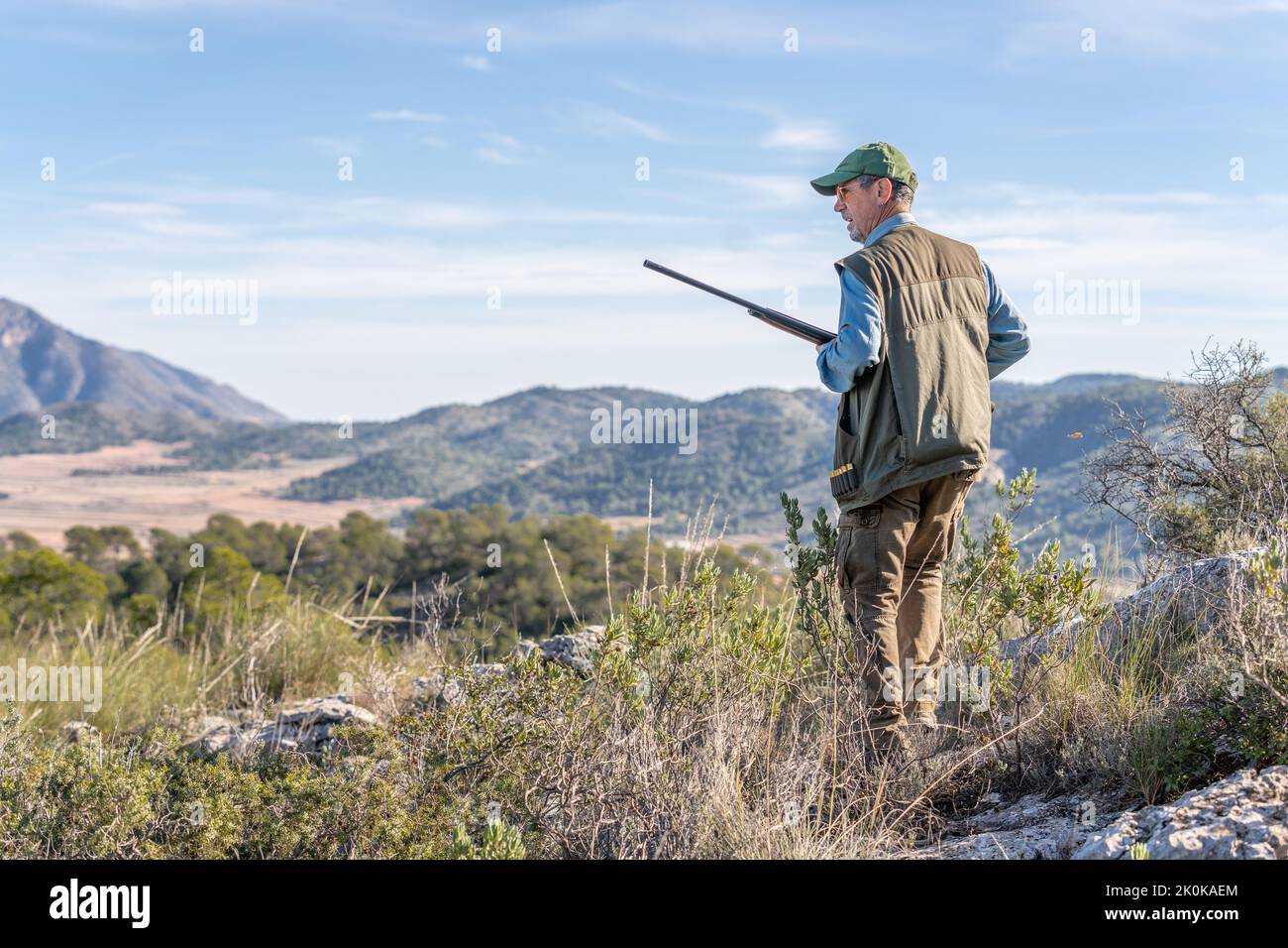 Side view of male hunter in special hunting vest and green cap holding ...