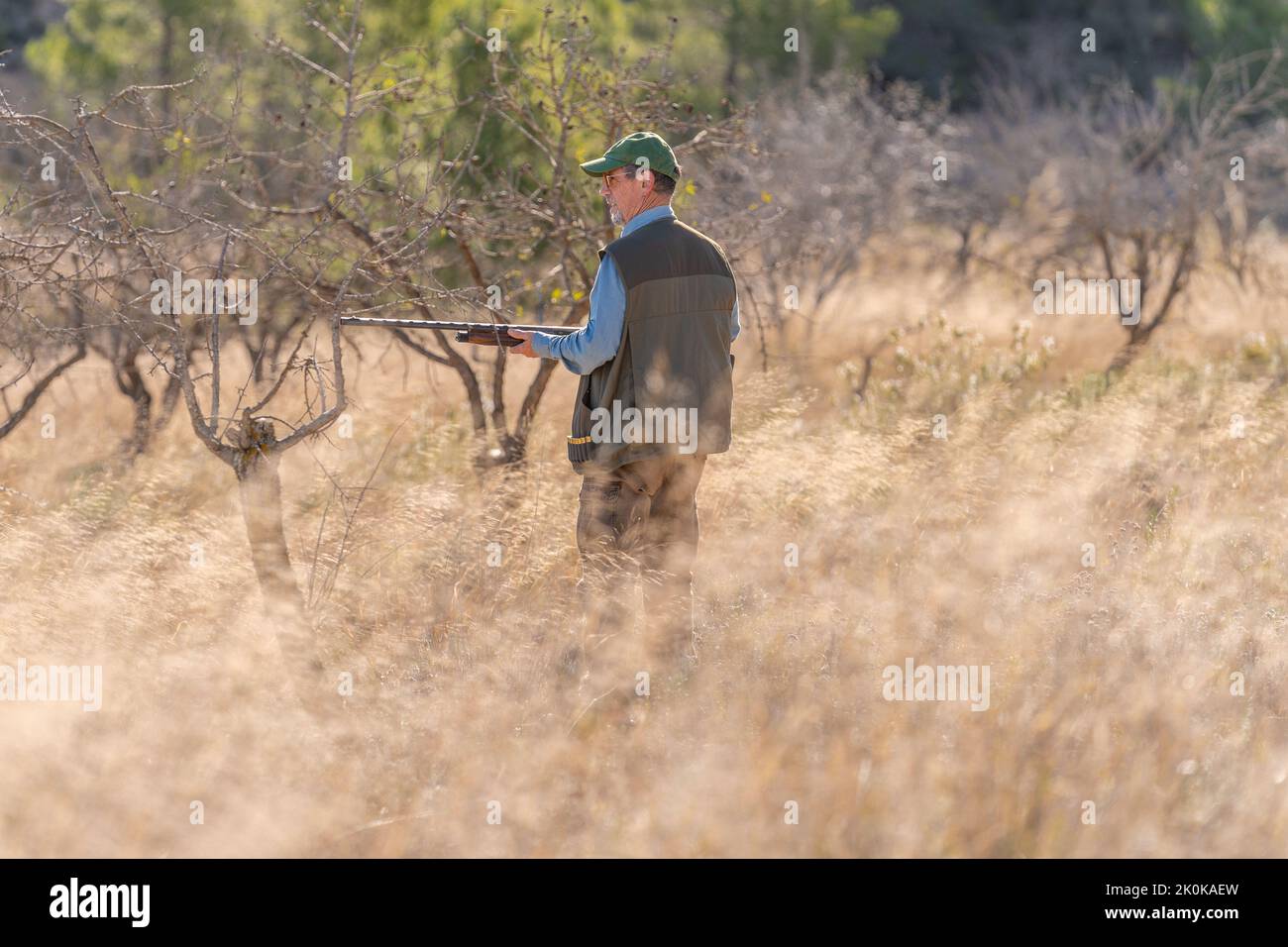 Side view of male hunter in special hunting vest and green cap holding ...