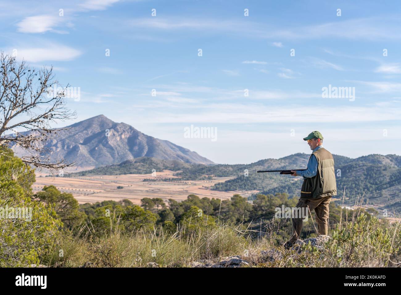 Side view of male hunter in special hunting vest and green cap holding ...