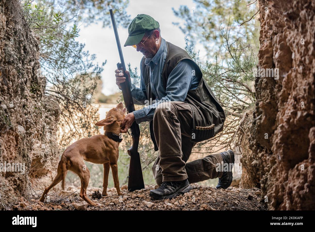 Side view of male hunter in camouflage wear and cap standing on knee ...