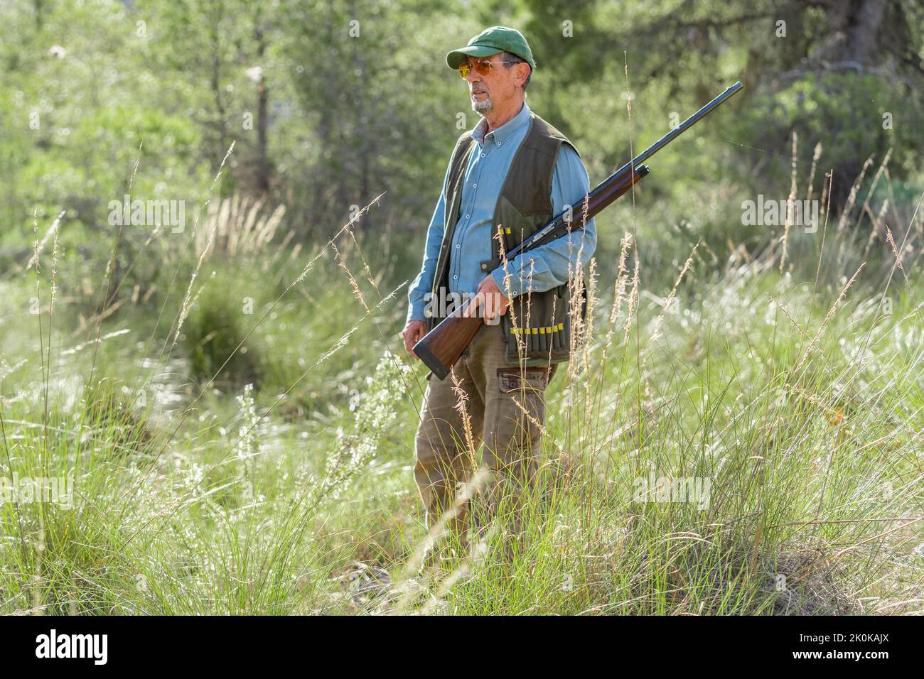 Male hunter in special hunting vest and green cap holding rifle and ...