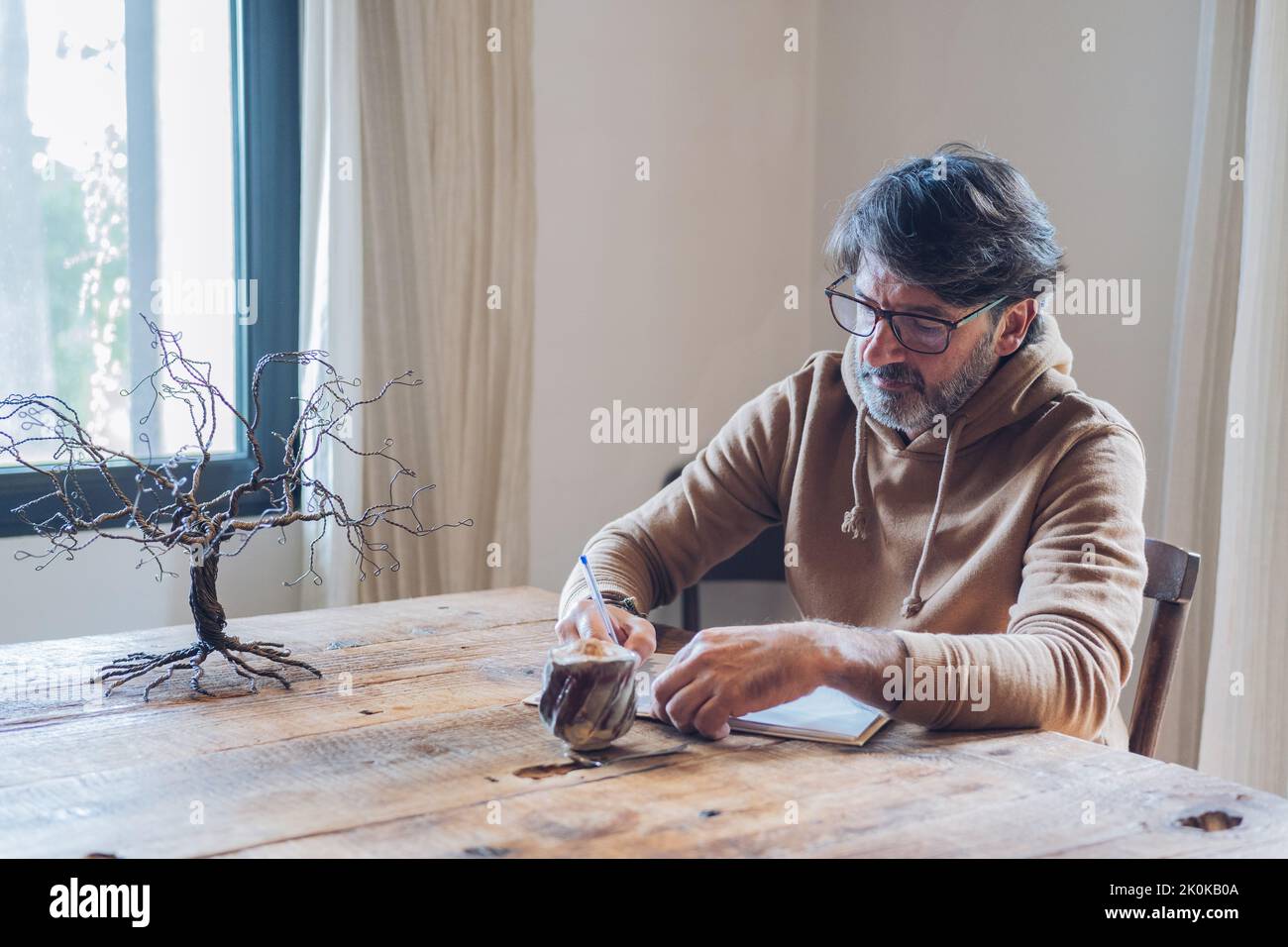 Side view of focused aged bearded male writing in notebook while ...