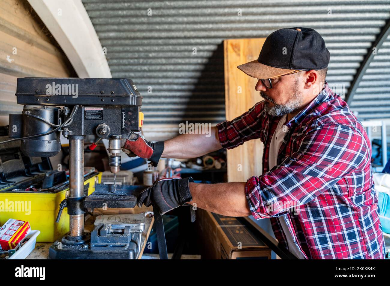 Side view of middle aged man in cap and plaid shirt working with wooden ...