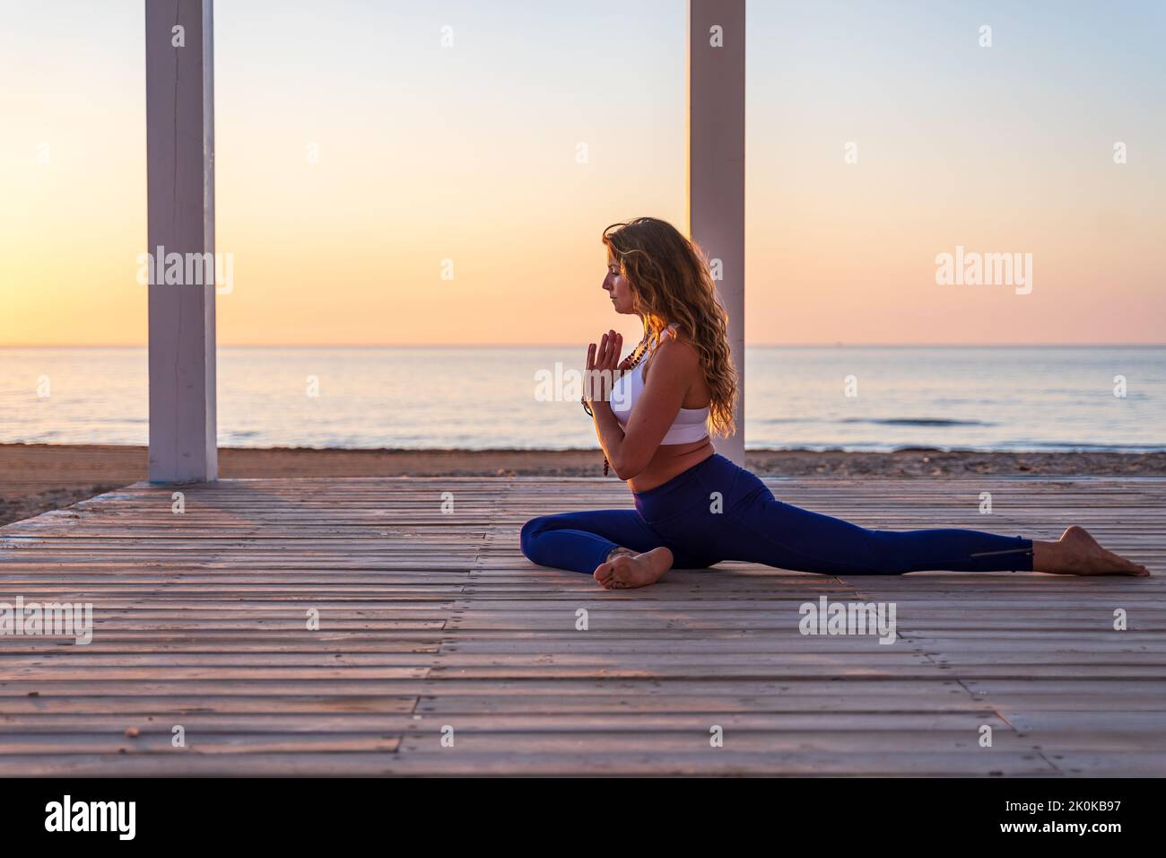 Side view of tranquil woman with Namaste gesture sitting on wooden ...