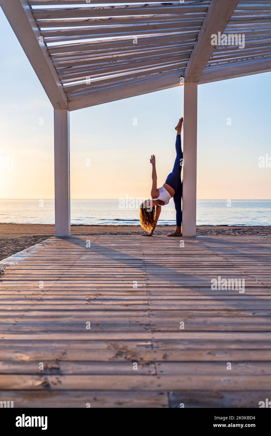 Side view of flexible female in sportswear balancing on leg and ...