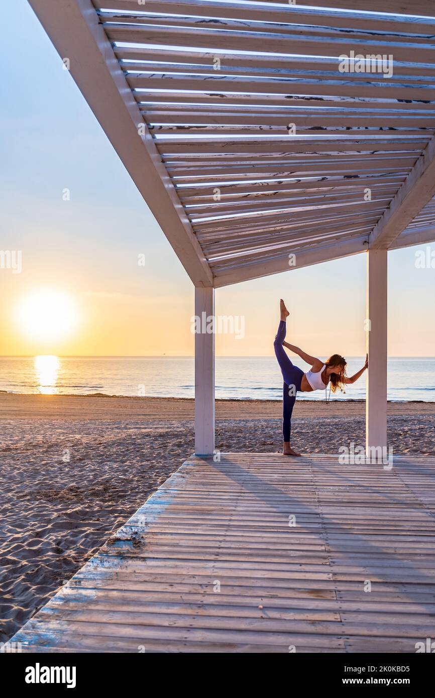 Side view of flexible female in sportswear balancing on leg and ...