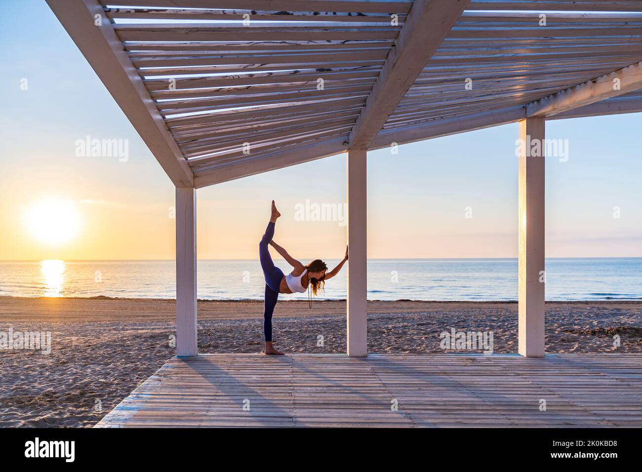 Side view of flexible female in sportswear balancing on leg and ...