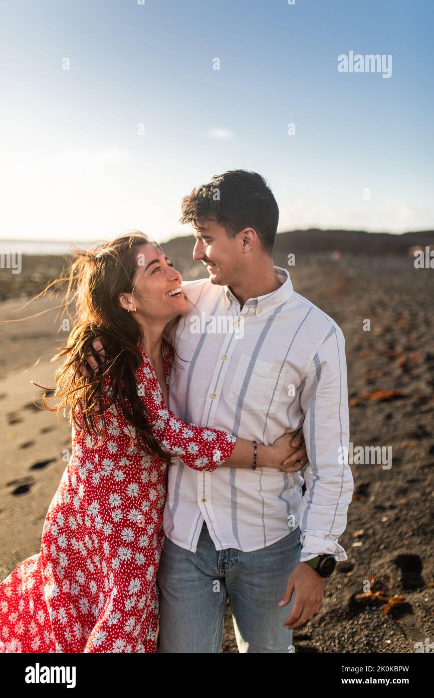 Side view of happy young ethnic female in stylish dress hugging back of ...