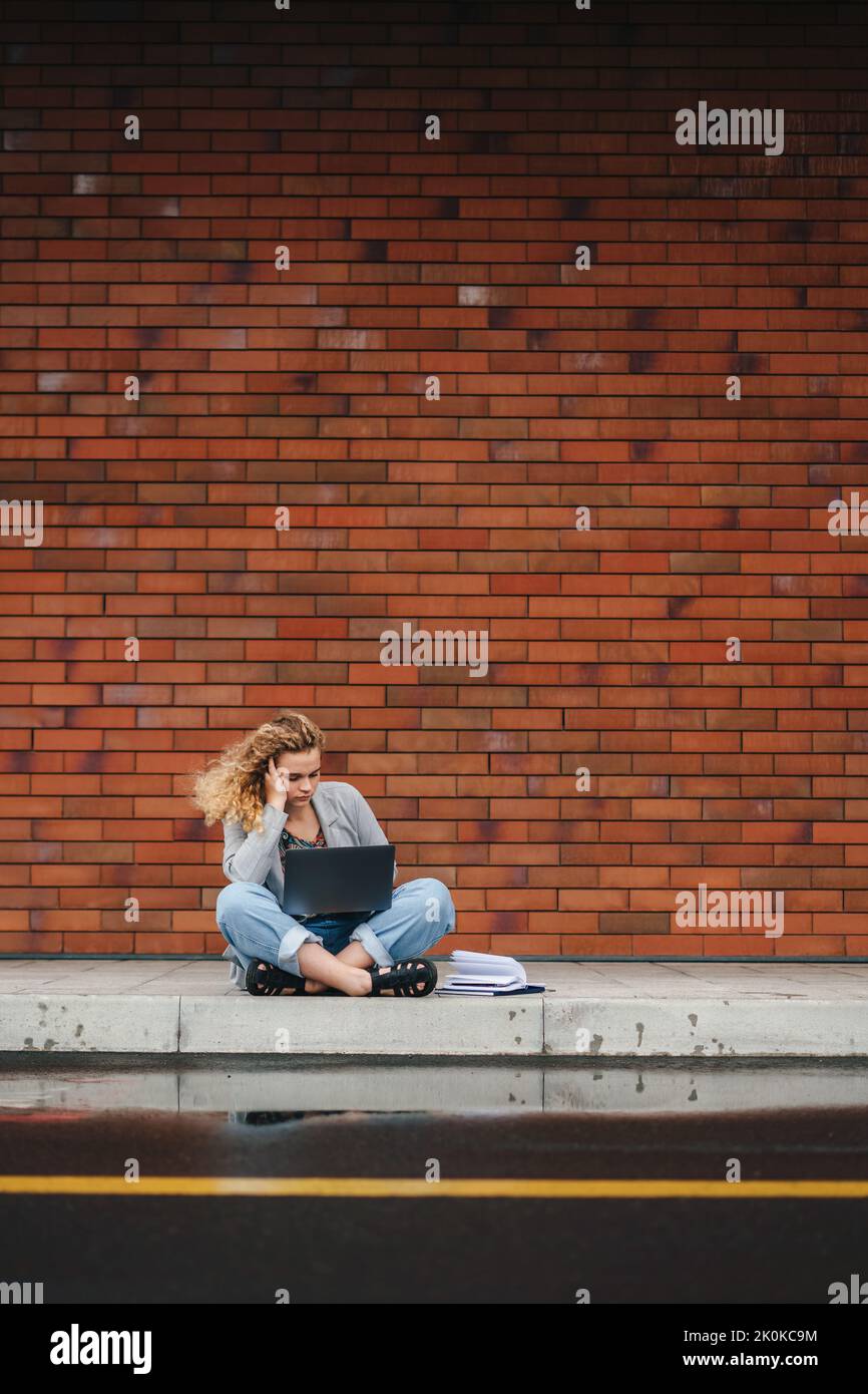 Distant view teen girl student using laptop computer modern technology device on city street ...