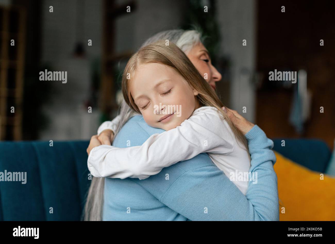 Smiling caucasian little girl with closed eyes and retired lady hugs ...
