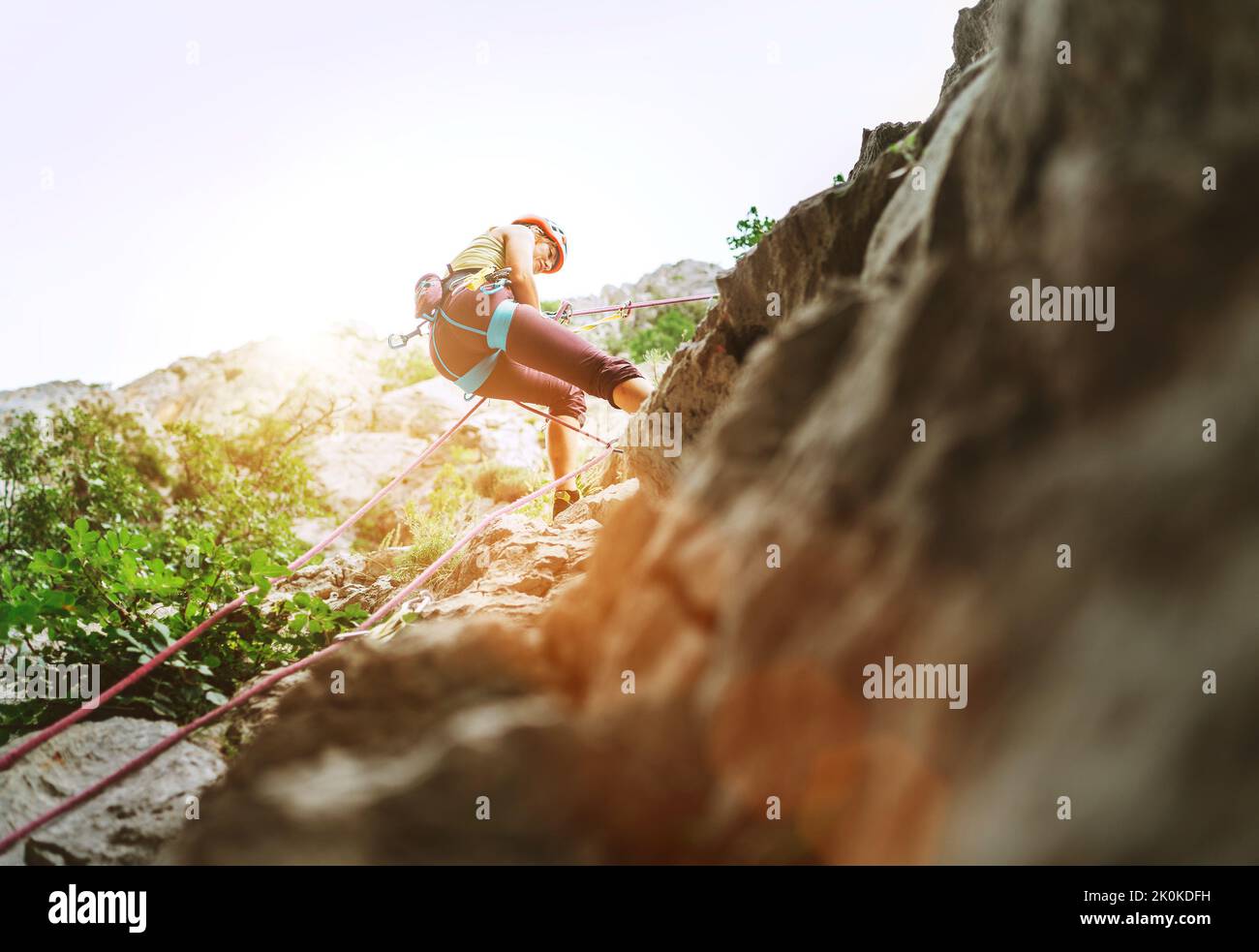 Active climber woman in protective helmet abseiling from cliff rock ...