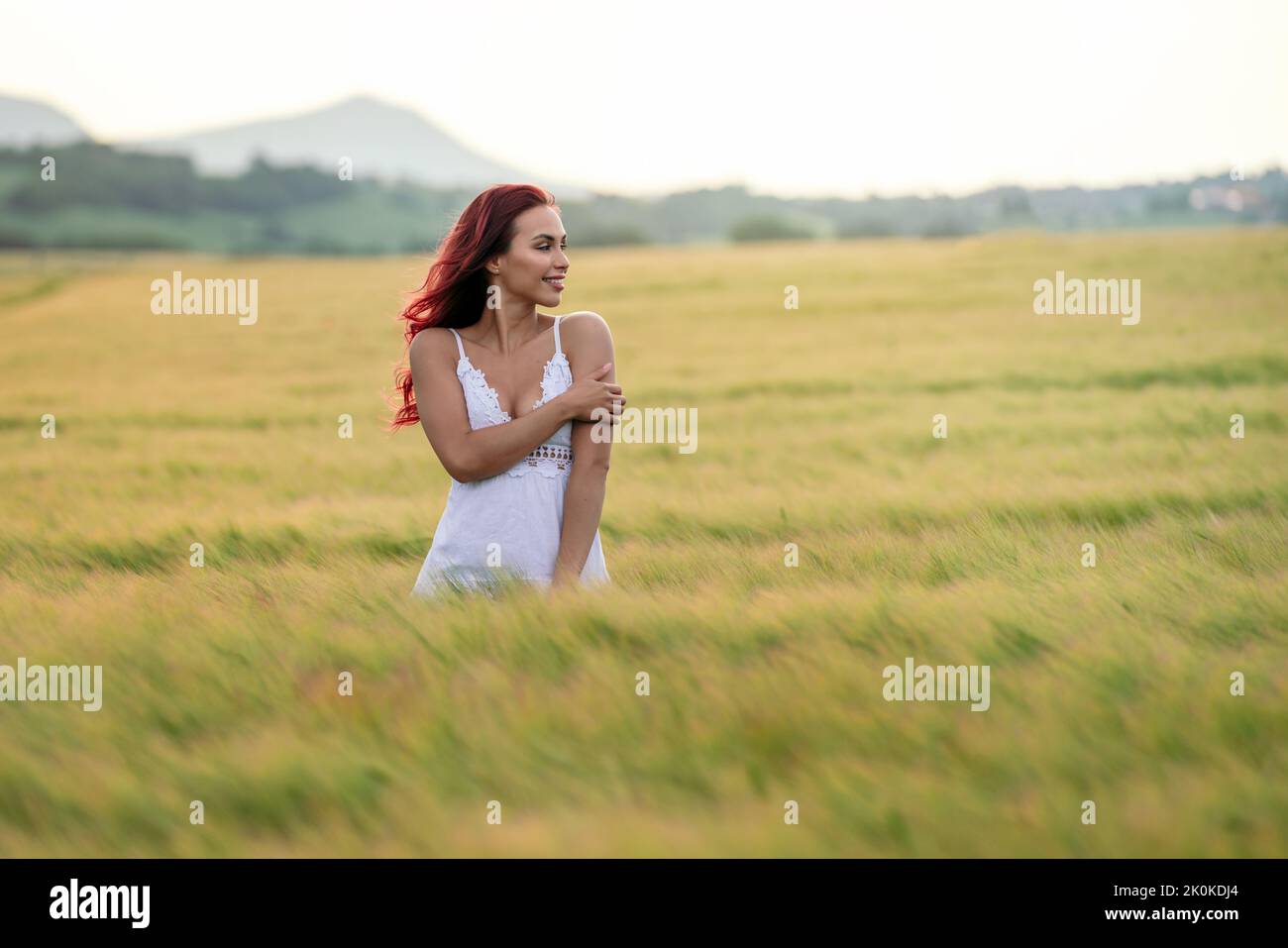 Young gentle female in white sundress touching arm while looking away ...