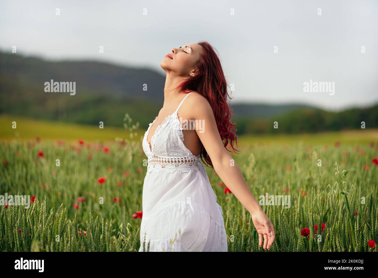 Side view of mindful woman with eyes closed in white sundress with red ...